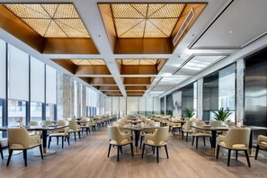 Uma sala de jantar ampla, com pé direito alto, grandes janelas e mobiliário moderno.