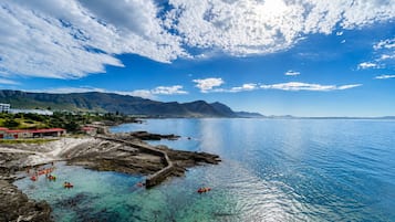Paisagem costeira com águas azul-claras, costas rochosas e montanhas ao longe.