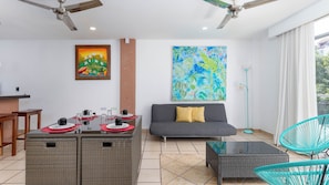 Uma sala de estar moderna com sofá, mesa de jantar com cadeiras, mesa de centro e ventilador de teto.