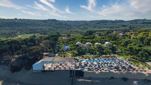Vista aérea de um resort com piscina, espreguiçadeiras e vista para as colinas ao redor.