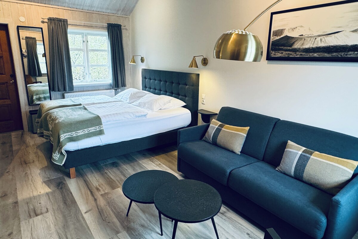 Quarto com uma cama de casal, um sofá azul, uma mesinha, um abajur e um quadro na parede.