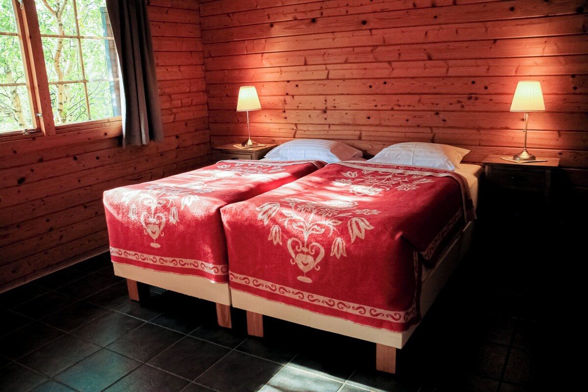 Quarto de cabana de madeira com duas camas, duas luminárias de cabeceira e uma janela com cortinas.