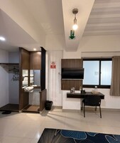 Uma sala de estar moderna com televisão de tela plana, área de jantar com mesa e cadeiras, um banco embutido e uma grande janela com cortinas.