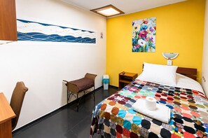 Quarto de hotel com cama, poltrona, mesa de cabeceira, quadro e placa de 'Proibido Estacionar'.