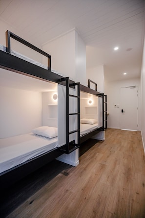Quarto com beliche, piso de madeira, paredes brancas e uma porta.