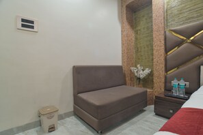 Quarto com cama, mesa de cabeceira com garrafas de água, lixeira e um respiradouro na parede.