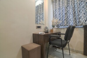 Um quarto com escrivaninha de madeira, uma cadeira, uma mesa pequena com um vaso de flores, um espelho e cortinas estampadas.