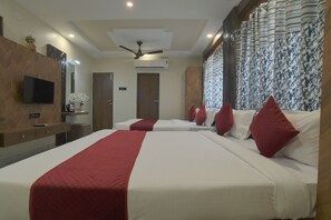 Quarto de hotel com três camas, televisão, ventoinha no teto e ar condicionado.