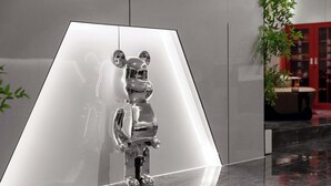 Escultura metálica de um urso em um saguão moderno, com piso refletivo e uma planta ao fundo.