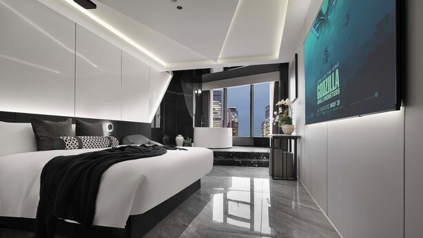 Quarto moderno com uma cama grande, vista para a cidade e um pôster de filme na parede.