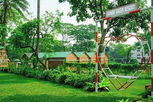 Placa para Namir Green Resort, rodeada por vegetação exuberante e uma estrutura de baloiço em formato de coração.