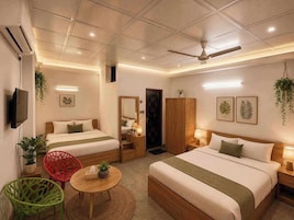 Quarto de hotel com duas camas, uma TV, um ventilador de teto e uma pequena mesa com uma planta.