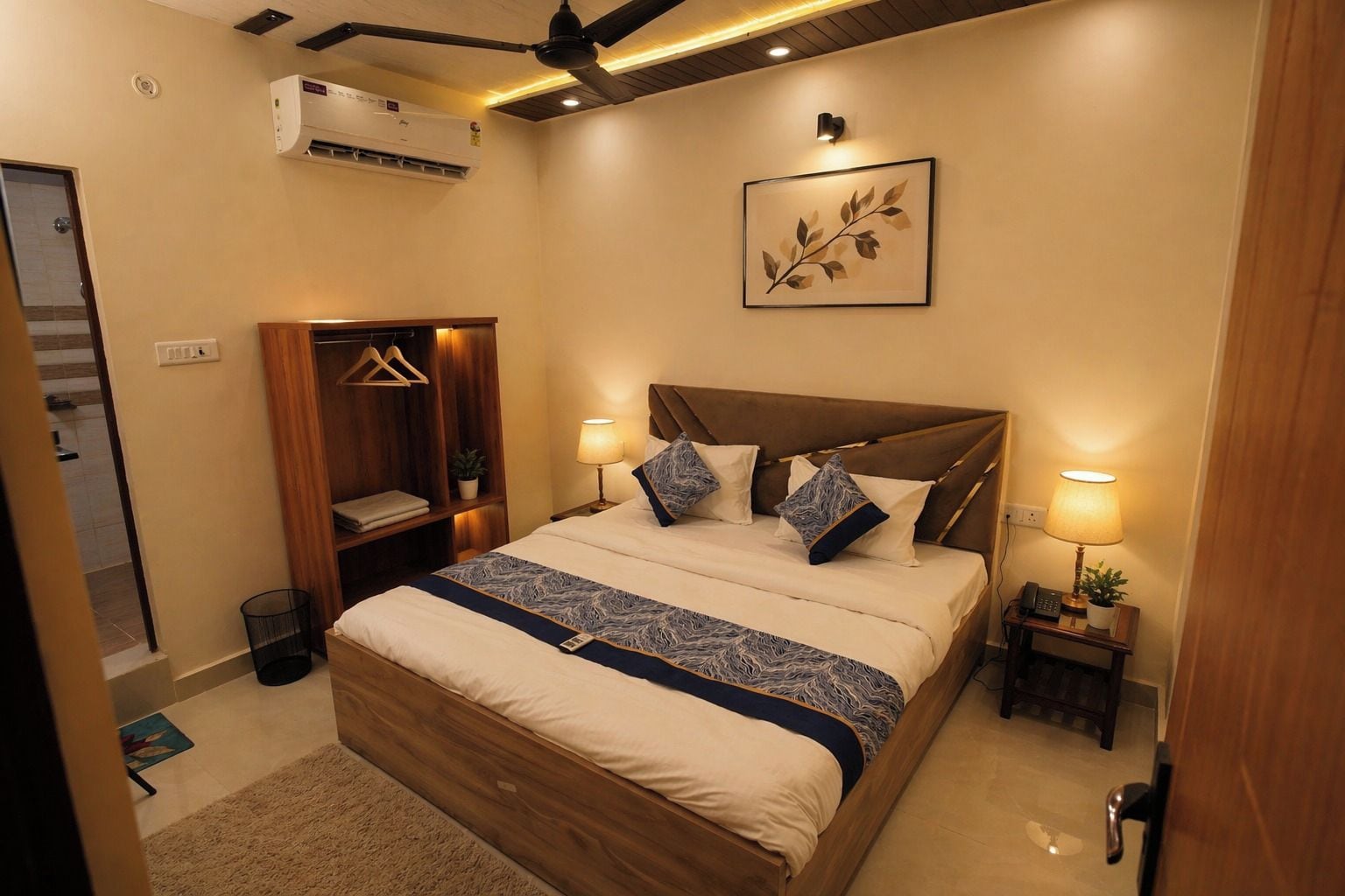 Quarto de hotel com cama, abajures, ar condicionado fixado na parede, cabideiro e uma obra de arte emoldurada.