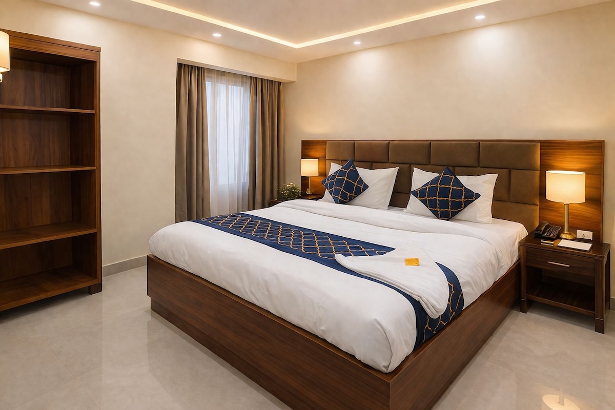 Quarto de hotel com uma cama grande, guarda-roupa de madeira, mesa de cabeceira com abajur e janela com cortinas.