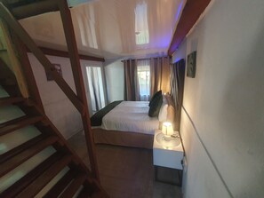 Um quarto com cama, mesa de cabeceira com abajur, janela com cortinas e escada.