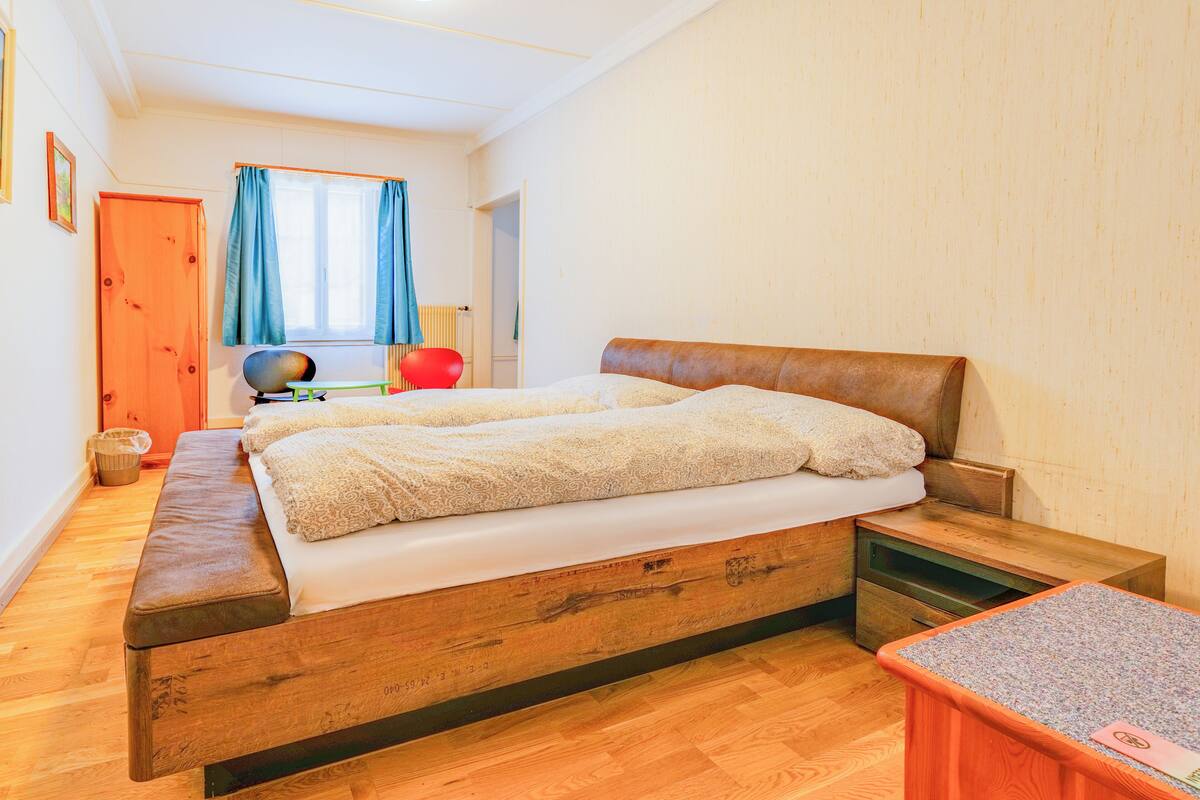 Uma cama de solteiro com estrutura de madeira, uma pequena mesa de cabeceira e um criado-mudo.