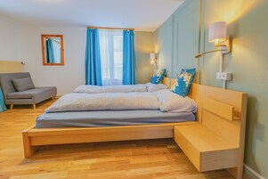 Quarto com cama de madeira, sofá cinzento, espelho e janela com cortinas azuis.