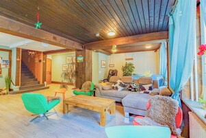 Uma sala de estar aconchegante com teto de madeira, escada, sofá, mesa de centro e janela com cortinas.