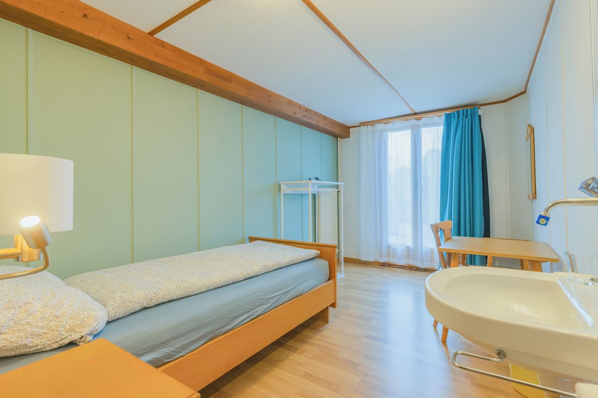 Quarto com cama, mesa de cabeceira, abajur e banheiro com pia e espelho.