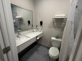 Casa de banho com lavatório branco, espelho, sanita e suporte para toalhas.