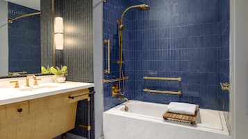 Casa de banho moderna com lavatório branco, detalhes dourados e zona de duche com azulejos azuis.