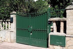 Um portão de metal verde com um cadeado, uma parede de pedra e uma caixa de metal à esquerda.