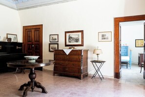 Um quarto com um piano, uma cômoda de madeira, uma mesinha com uma tigela e quadros nas paredes.