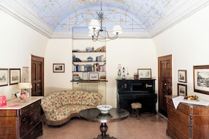 Um quarto com sofá curvo, mesa redonda, estante de livros, piano e quadros nas paredes.