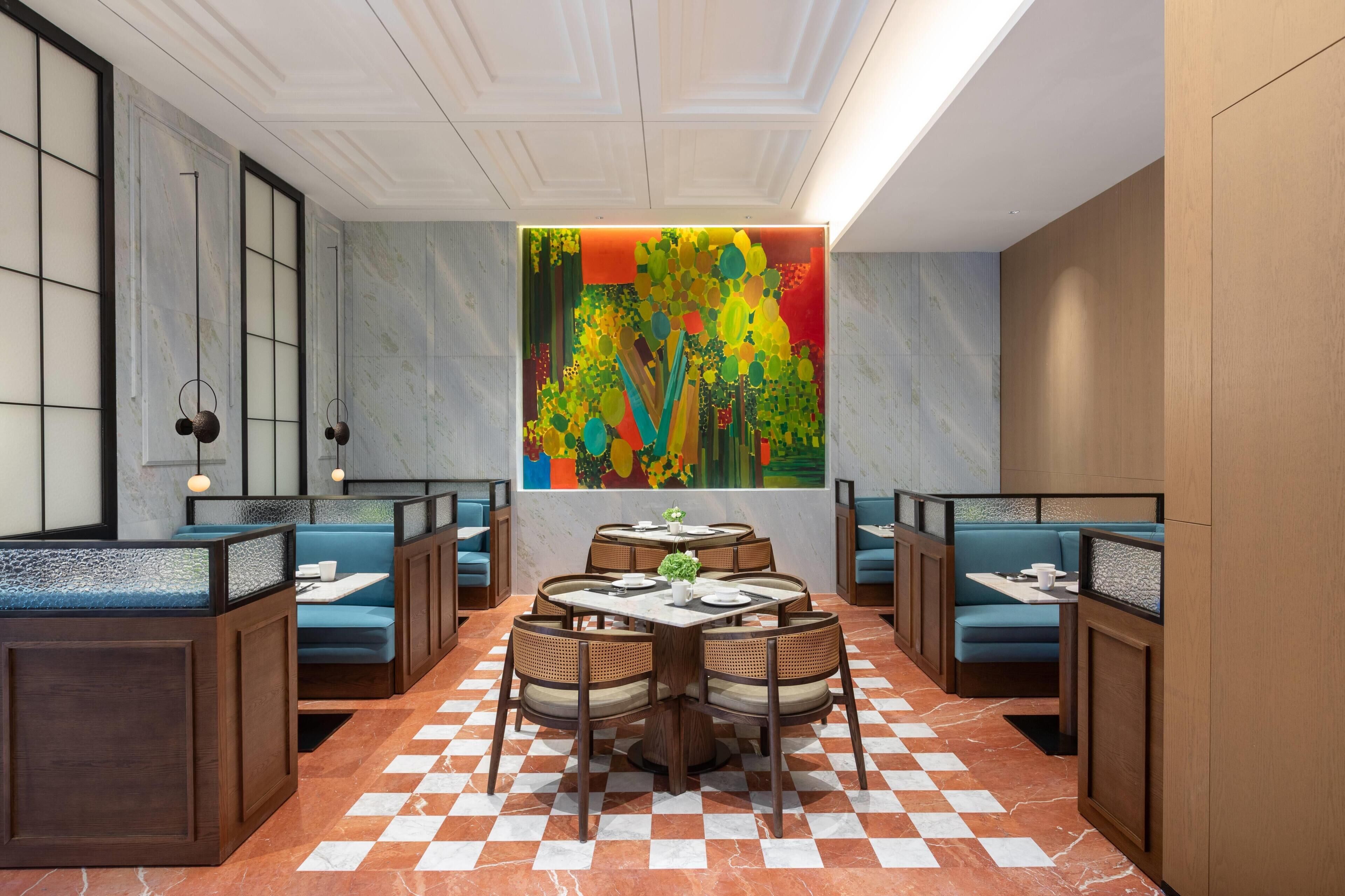 Um restaurante com chão quadriculado, assentos em cabines de madeira e uma pintura abstrata colorida na parede.