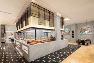 Um lobby de hotel moderno com área de buffet central, piso de mármore e obras de arte contemporâneas.