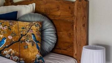 Uma cama de madeira com travesseiro floral, uma mesa redonda com abajur e um espelho na parede.