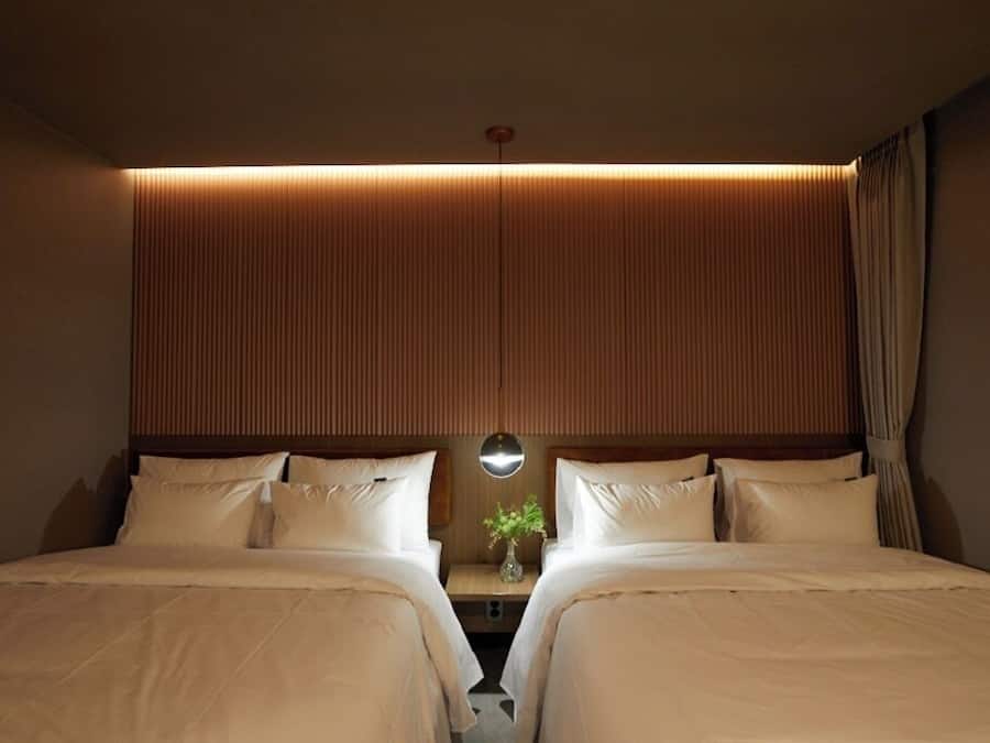 Quarto de hotel com duas camas, uma mesa de cabeceira com um vaso e um espelho na parede.
