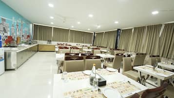 Área de refeições com mesas preparadas para o serviço, cozinha e um mural na parede.