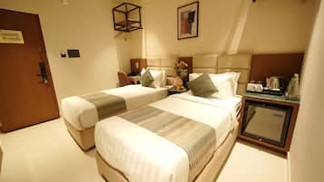 Quarto de hotel com duas camas, uma escrivaninha, um pequeno frigorífico e uma prateleira na parede.
