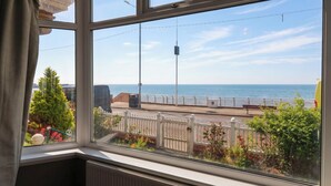 Quarto com vista para o mar através de uma grande janela, um corrimão branco na parte externa e um radiador abaixo da janela.