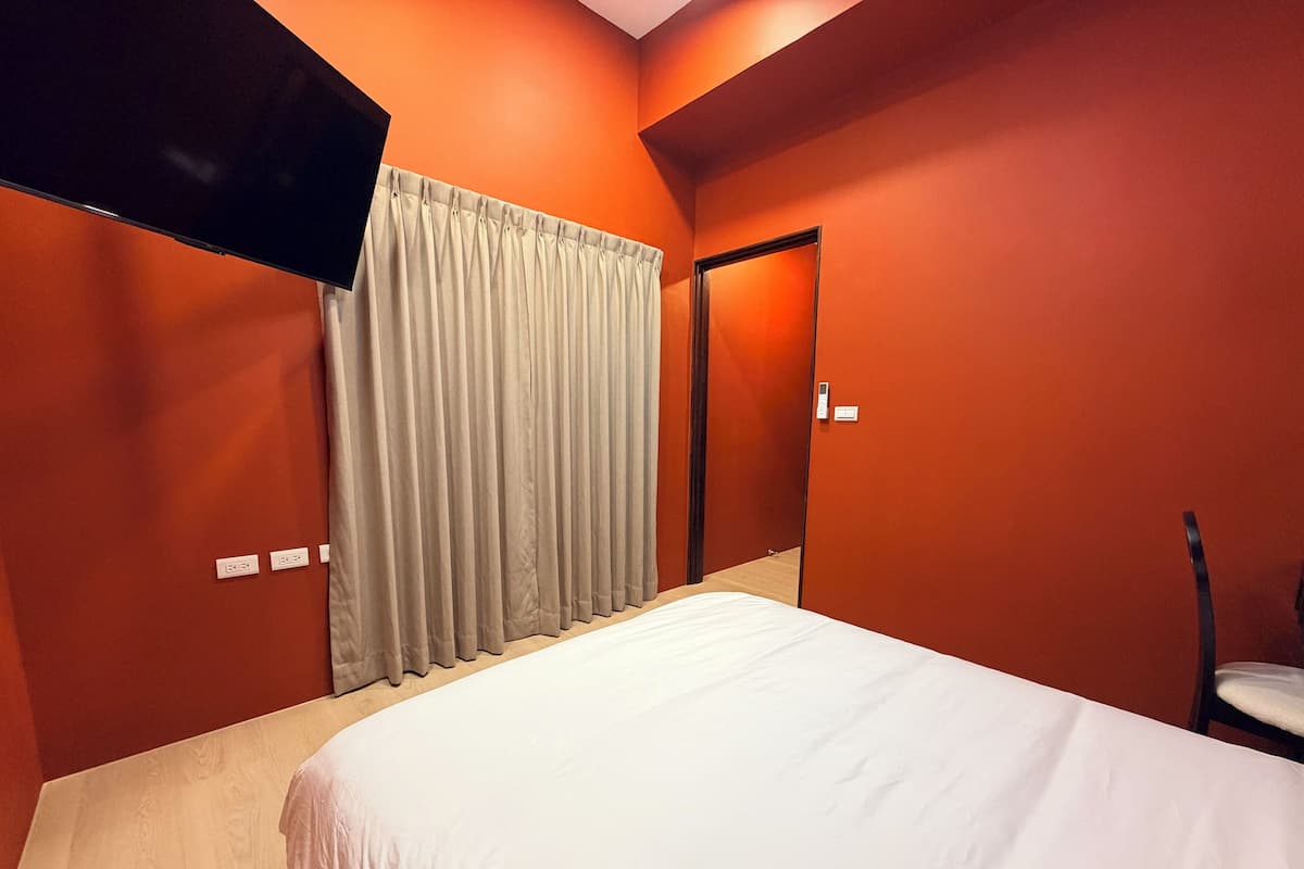 Quarto de hotel com uma cama, uma televisão fixada na parede e uma porta com espelho.