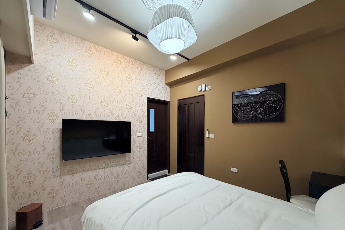 Quarto de hotel com uma cama grande, uma televisão de tela plana na parede, uma porta e um aplique.