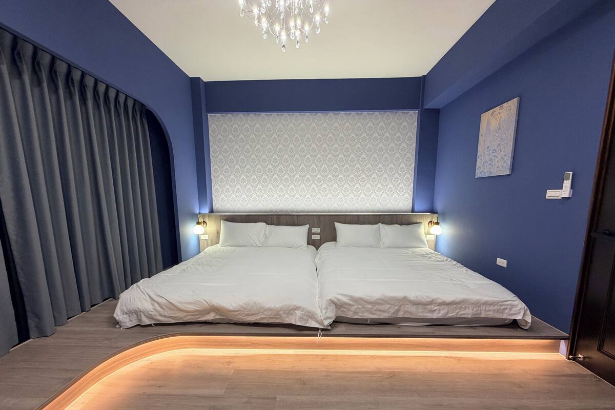 Uma cama de casal com cabeceira de madeira, parede estampada e um lustre.