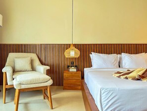 Quarto de hotel com cama, uma cadeira, mesa de cabeceira e luminária.