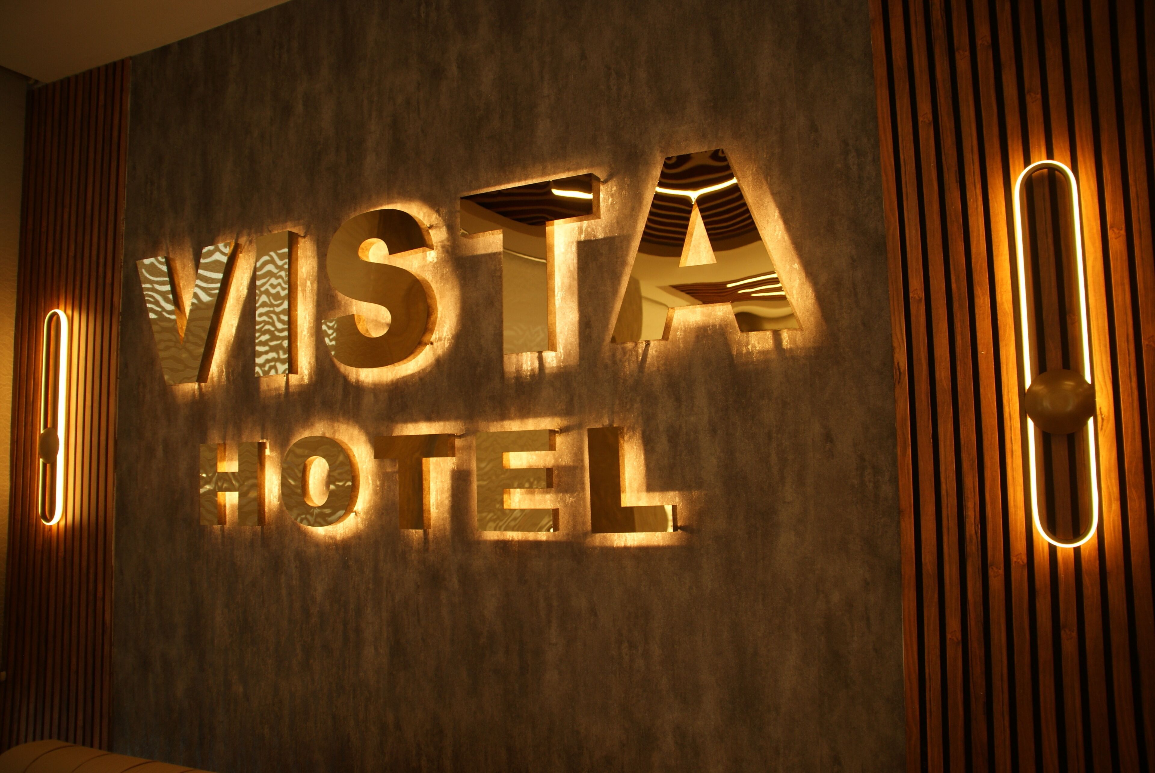 Pareda com letras iluminadas formando a palavra 'VISTA HOTEL'.