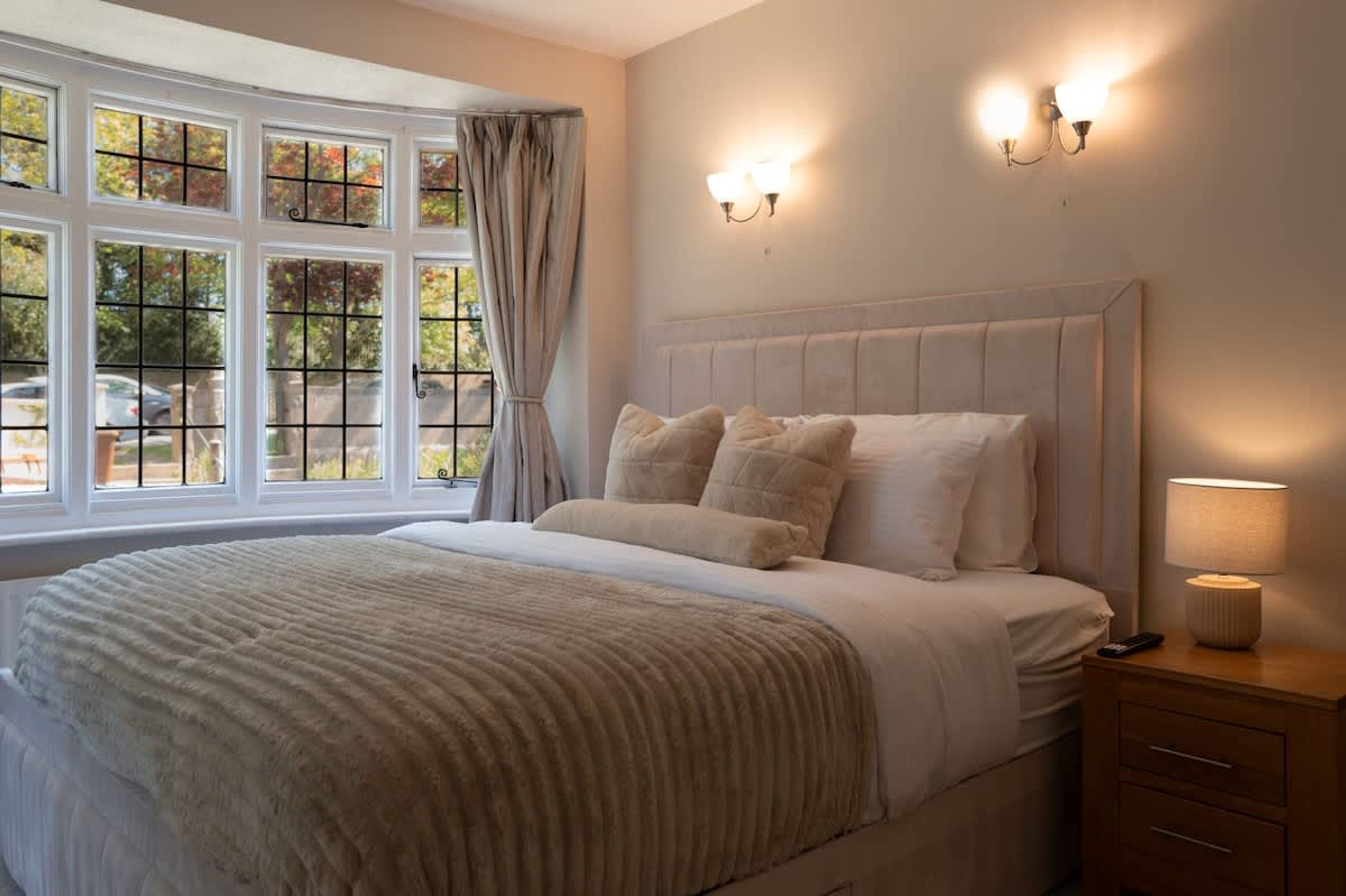 Quarto com uma cama grande, mesa de cabeceira com abajur e janela com cortinas.