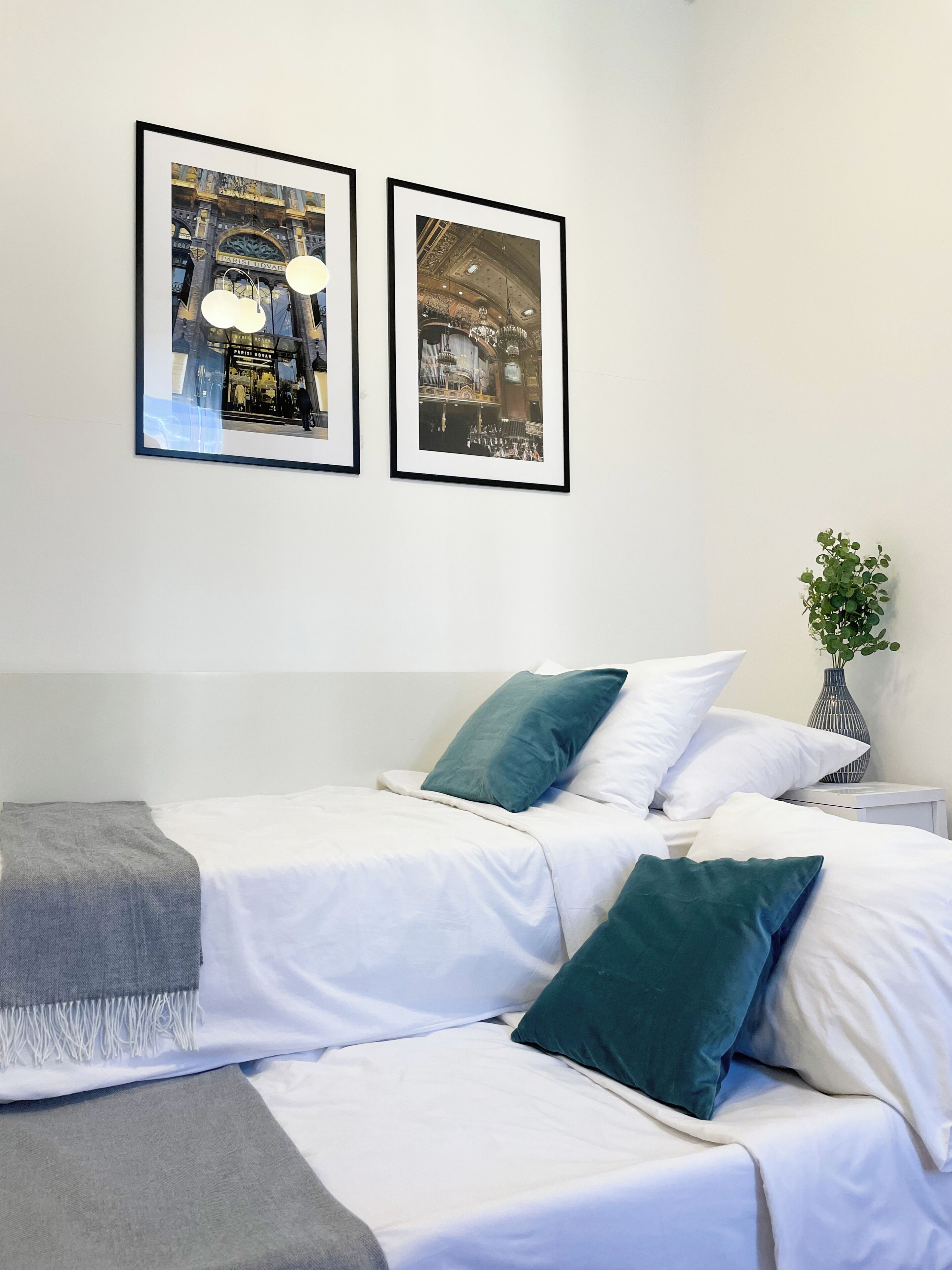 Quarto com duas camas, mesa de cabeceira, planta em vaso e duas quadros na parede.