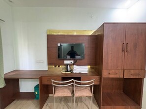 Quarto com escrivaninha de madeira, duas cadeiras, televisão fixada na parede e um armário.