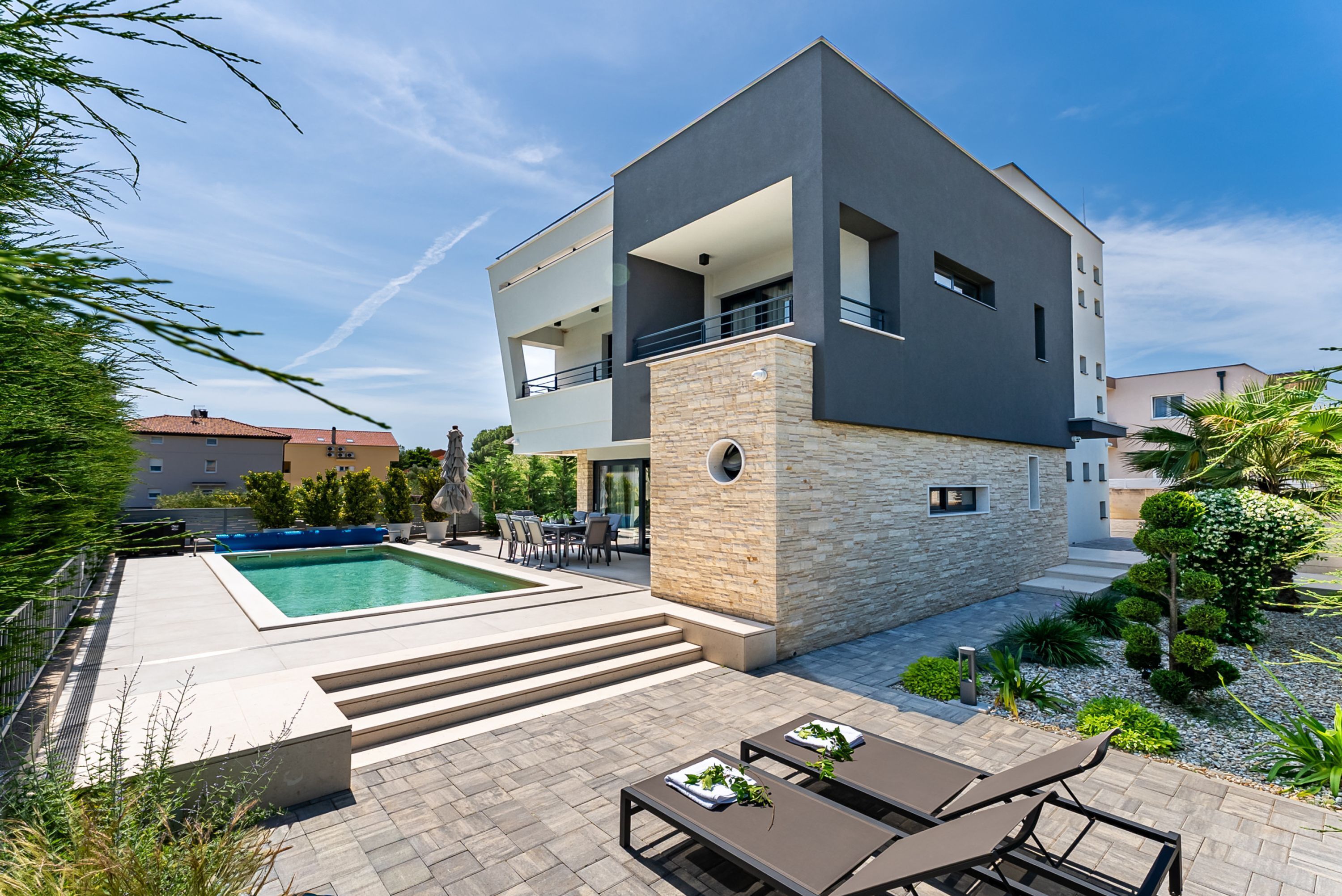 Uma casa moderna de dois andares com piscina, área de estar externa e fachada de pedra.