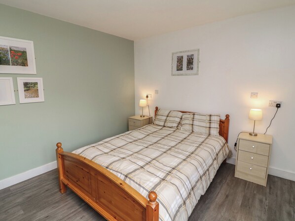 Quarto com cama de madeira, duas mesas de cabeceira com luminárias, um pequeno aparador e quadros nas paredes.