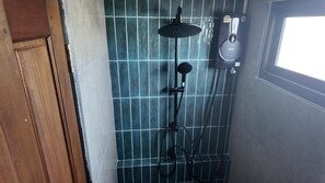 Um banheiro com chuveiro, um chuveiro manual e um painel de controle fixado na parede.