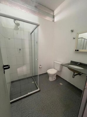 Casa de banho com cabine de duche em vidro, sanita e lavatório com espelho.