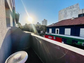 Uma varanda com uma cadeira, um edifício com a placa 'DENTISTAS' e um céu claro com o sol.