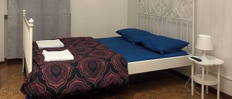 Quarto com cama, mesa de cabeceira, abajur, cortina e quadro na parede.