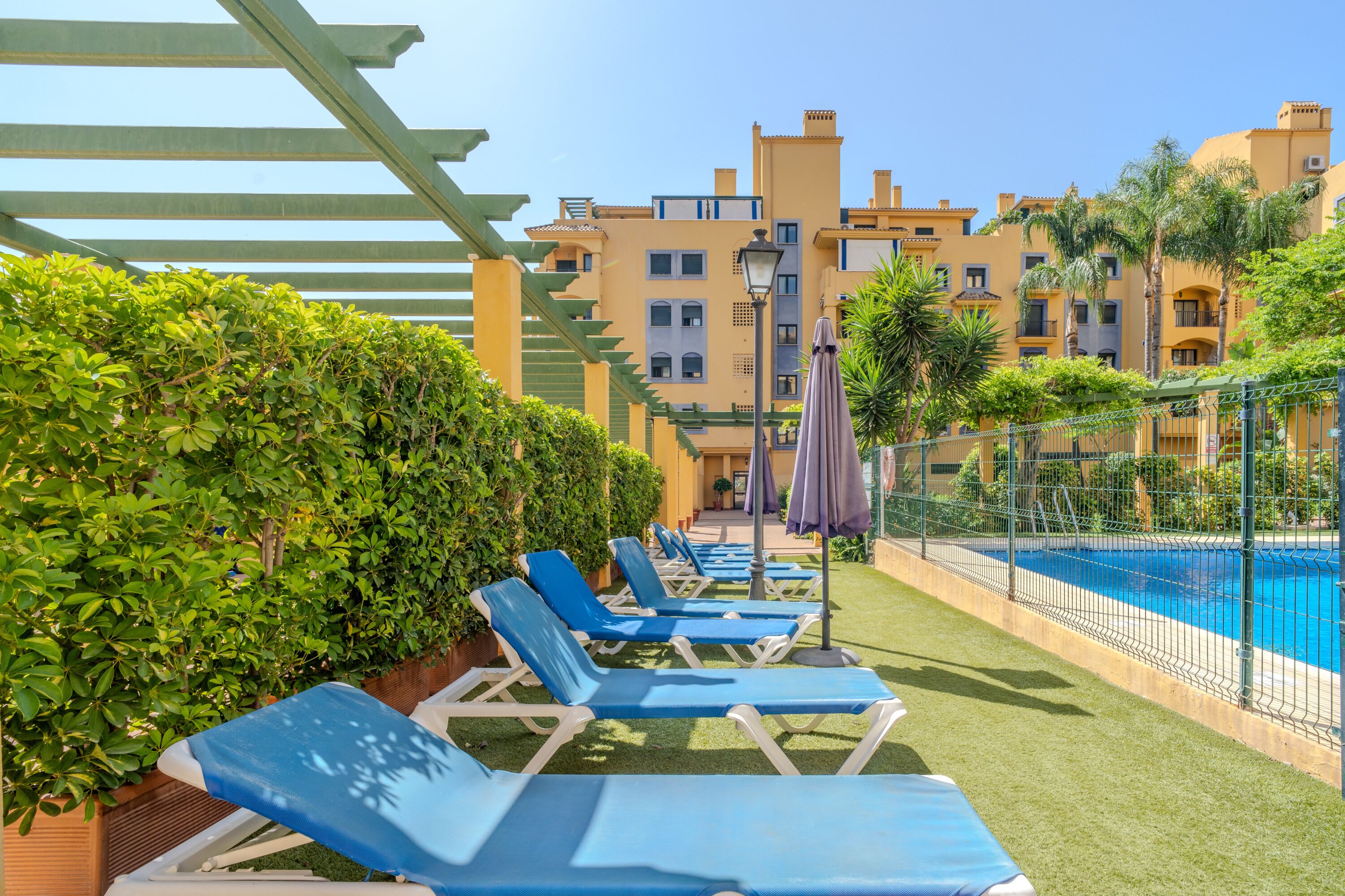 Uma área na piscina com espreguiçadeiras, piscina e um edifício com varandas.